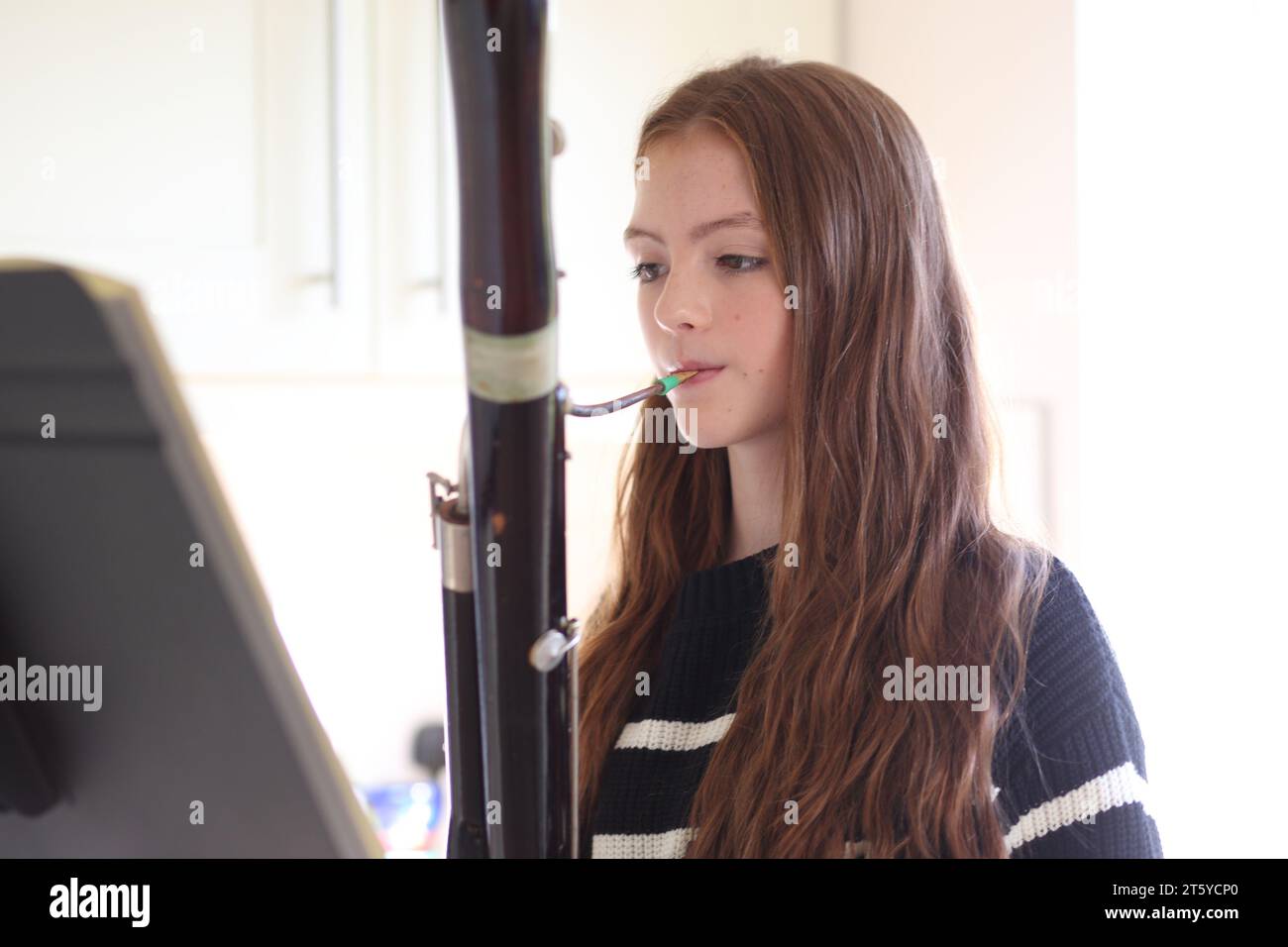 Teenage girl playing the bassoon in kitchen at home. Plays musical ...