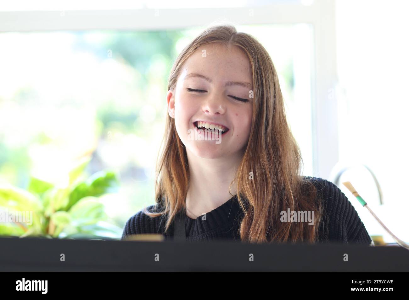 Teenage girl playing the bassoon in kitchen at home. Laughing as she ...