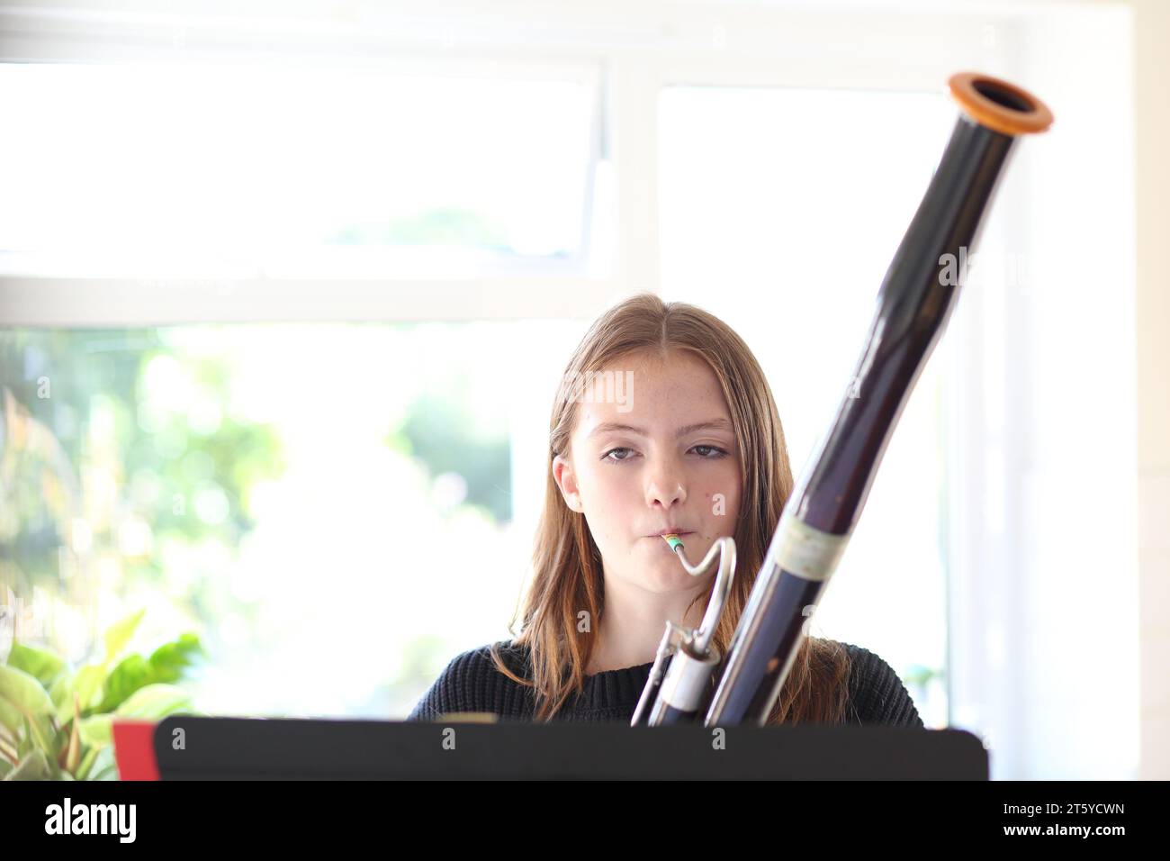 Teenage girl bassoon player in kitchen at home. Plays musical scales ...