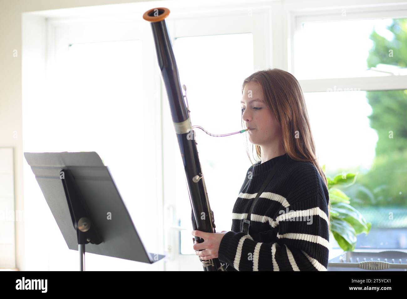 Teenage girl playing the bassoon in kitchen at home. Plays musical ...