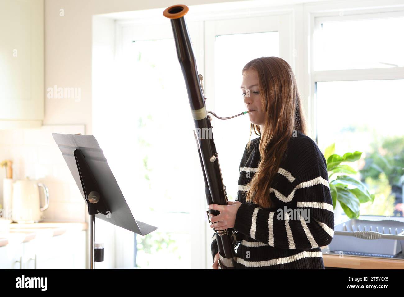 Teenage girl bassoon player in kitchen at home. Plays musical scales ...