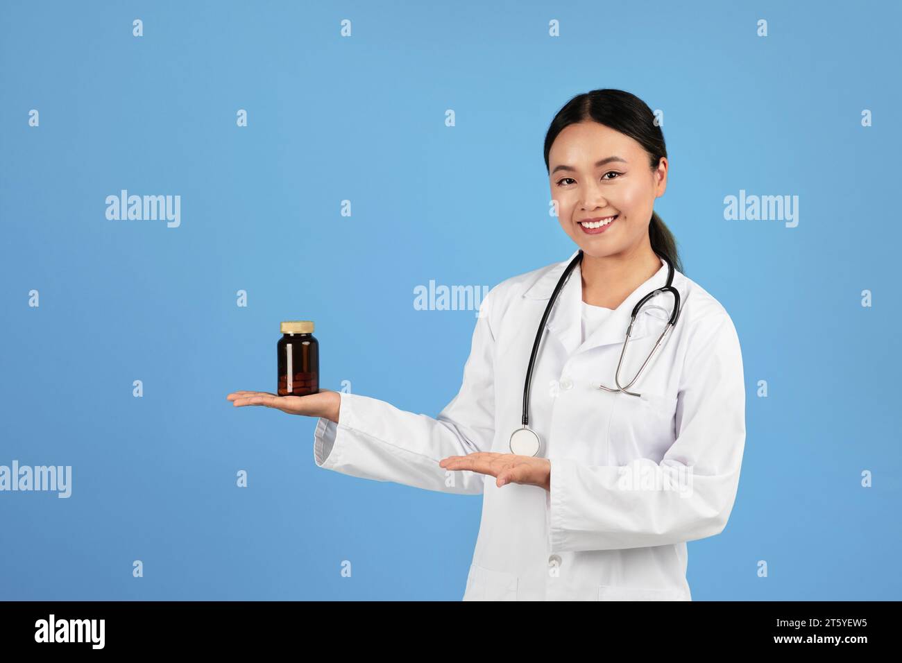 Smiling young asian doctor woman in white coat holding jar of medicines ...