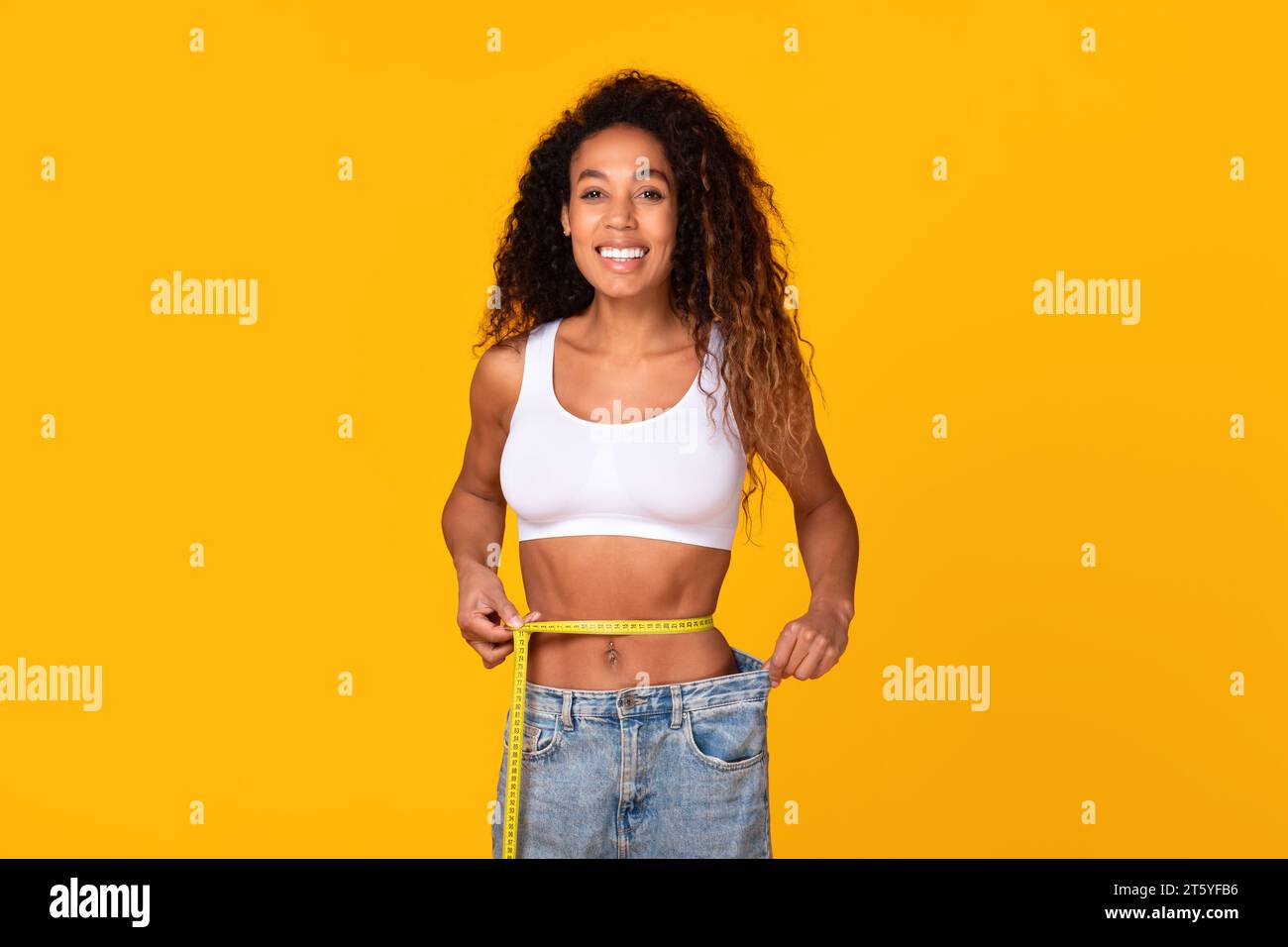 Slim african lady measuring waist with tape over yellow backdrop Stock ...