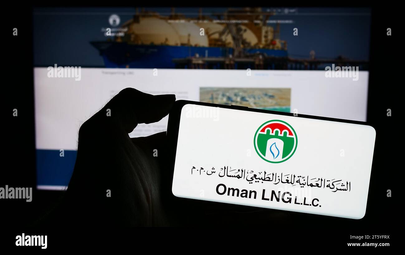 Person holding cellphone with logo of Omani liquefied natural gas ...
