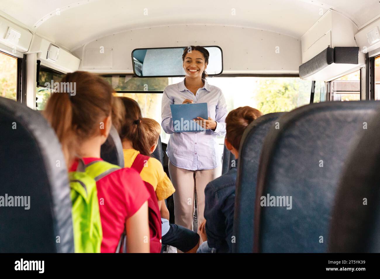 Friendly black female teacher checking off children names sitting inside school bus Stock Photo ...
