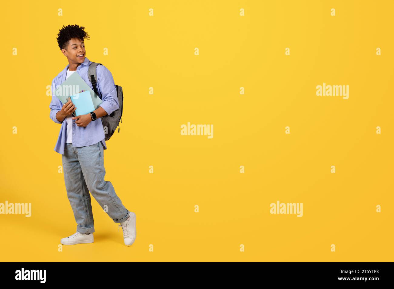 Happy black male student walking with notebooks, looking at free space ...