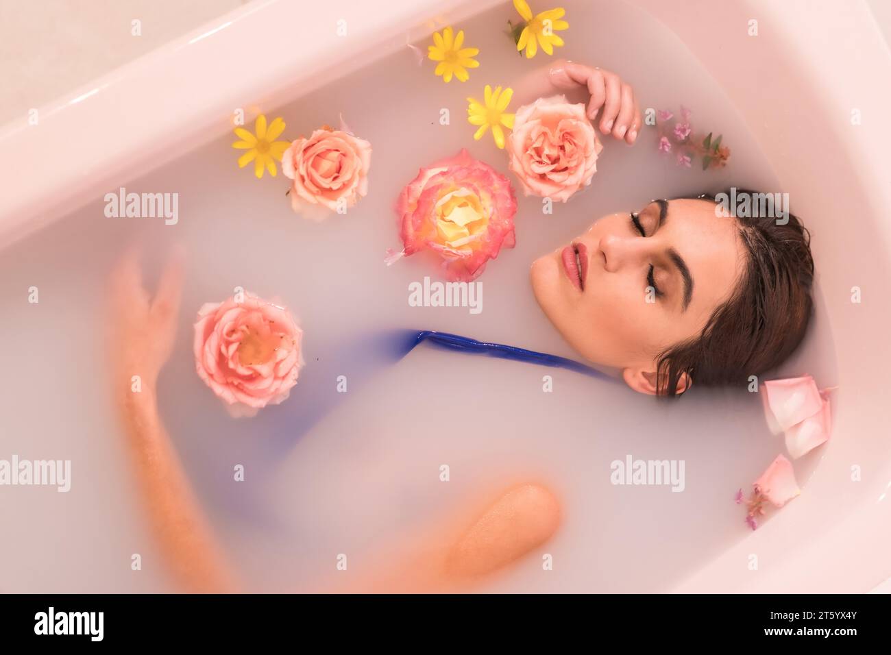 Artistic portrait from above of a model taking a milk bath with flowers ...
