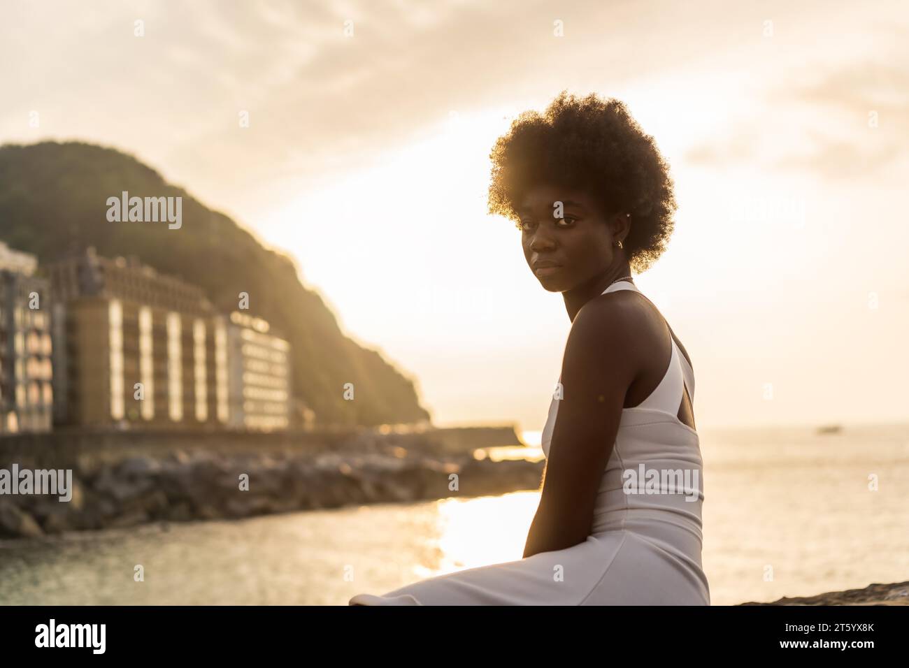 Afro beauty woman turning to look at camera while gazing the ocean ...