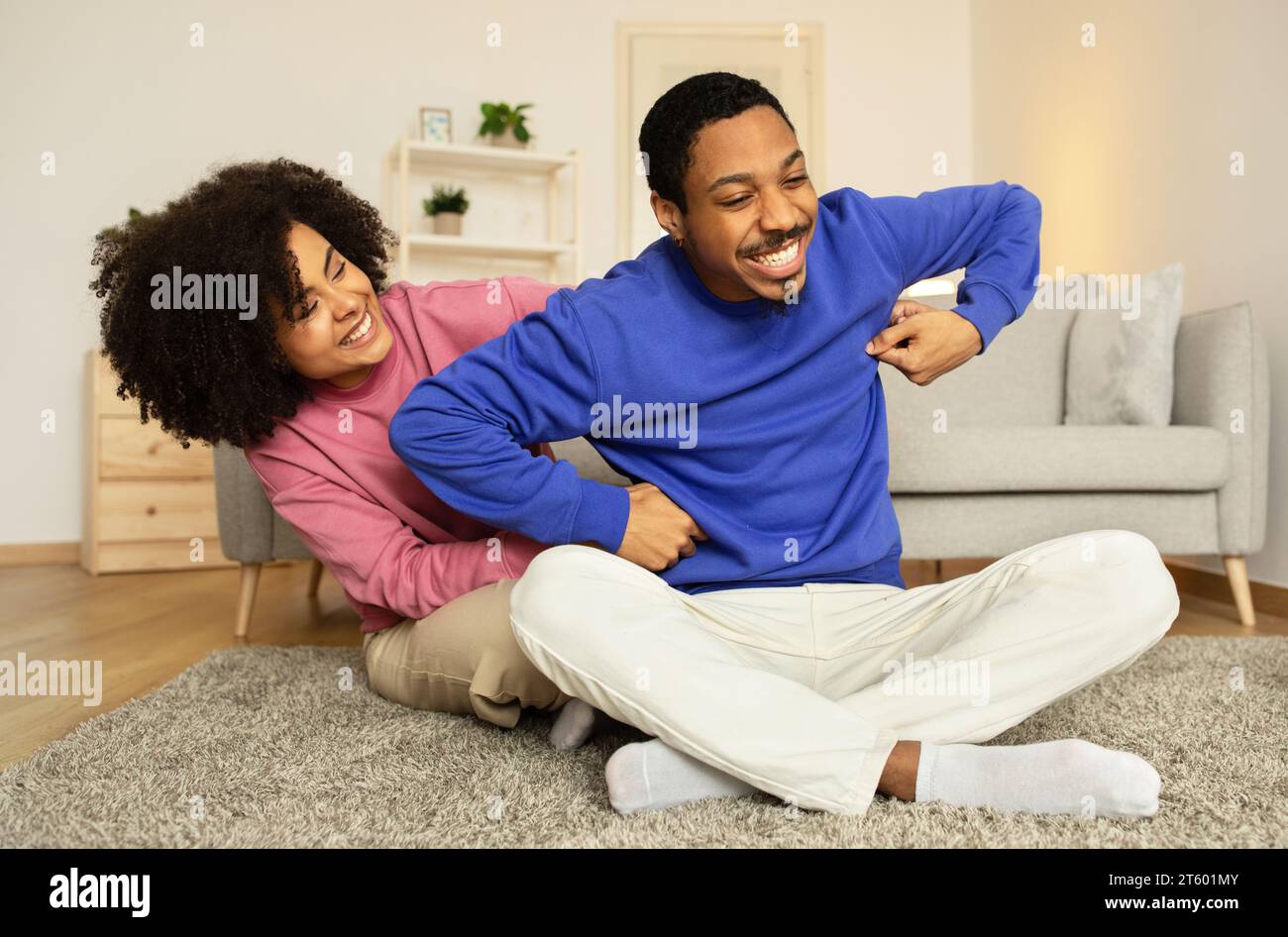 Cheerful black wife bonding with husband through gentle tickles indoor ...