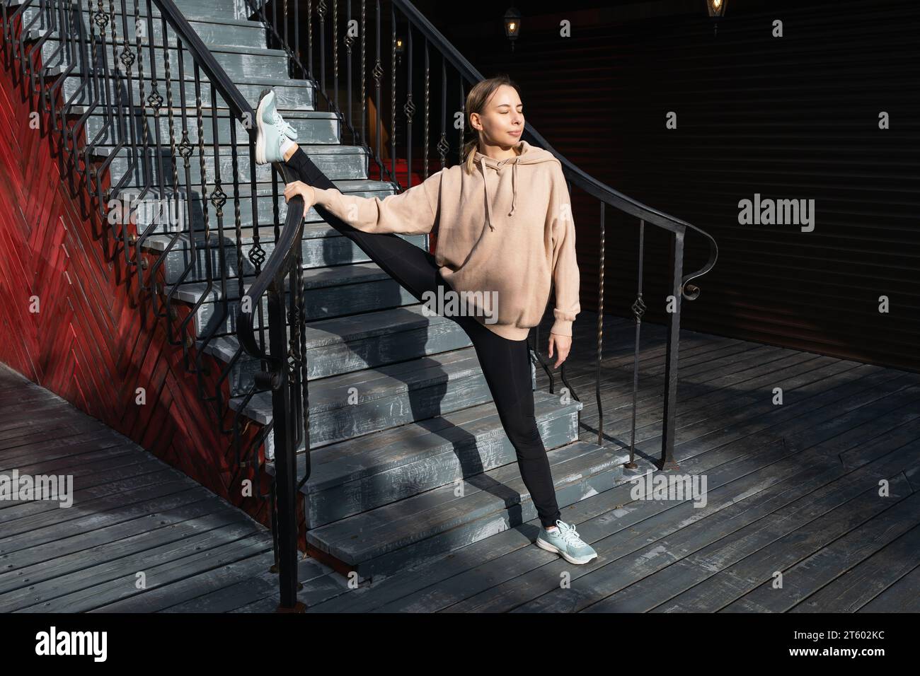 A young attractive woman trains in sportswear on the street, stretches ...