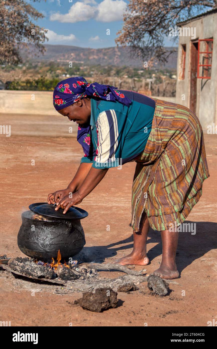 african woman cooking boiling outdoors some meat setswa on a three ...