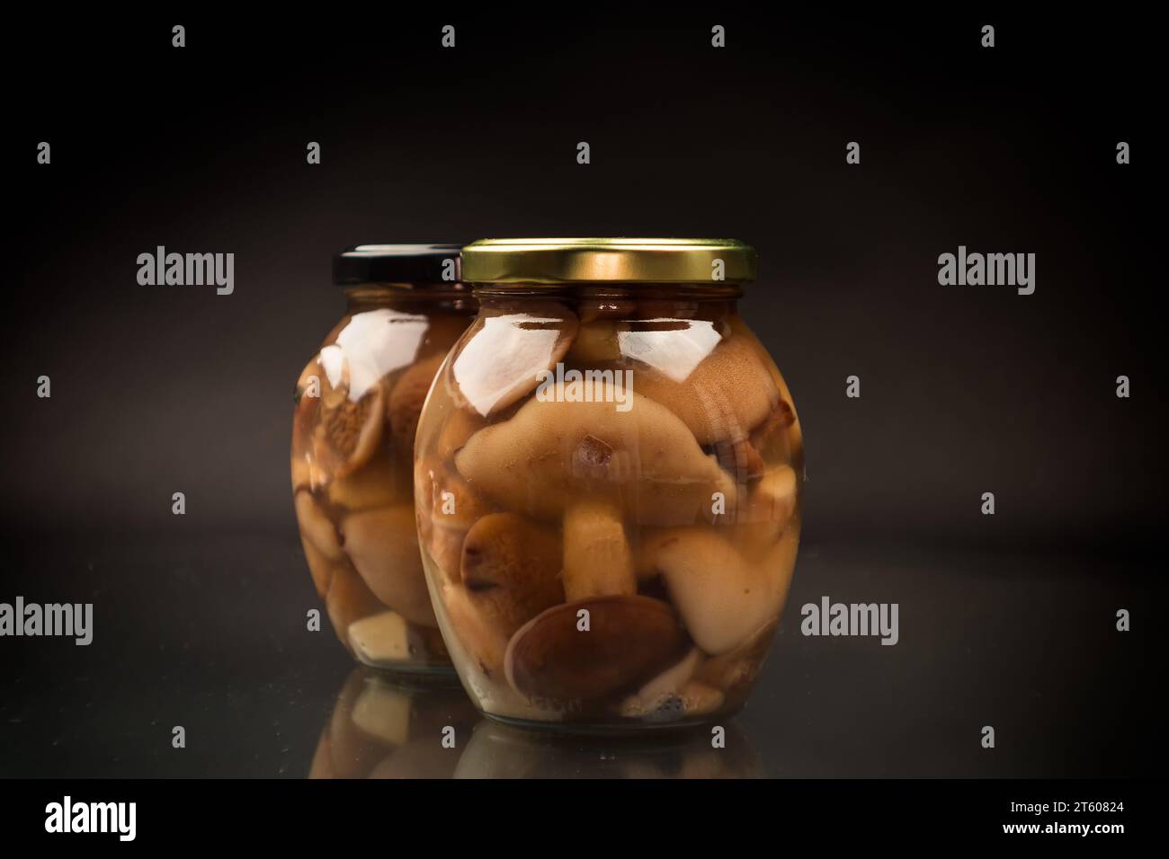 pickled wild boletus mushrooms in a glass jar, isolated on a black ...