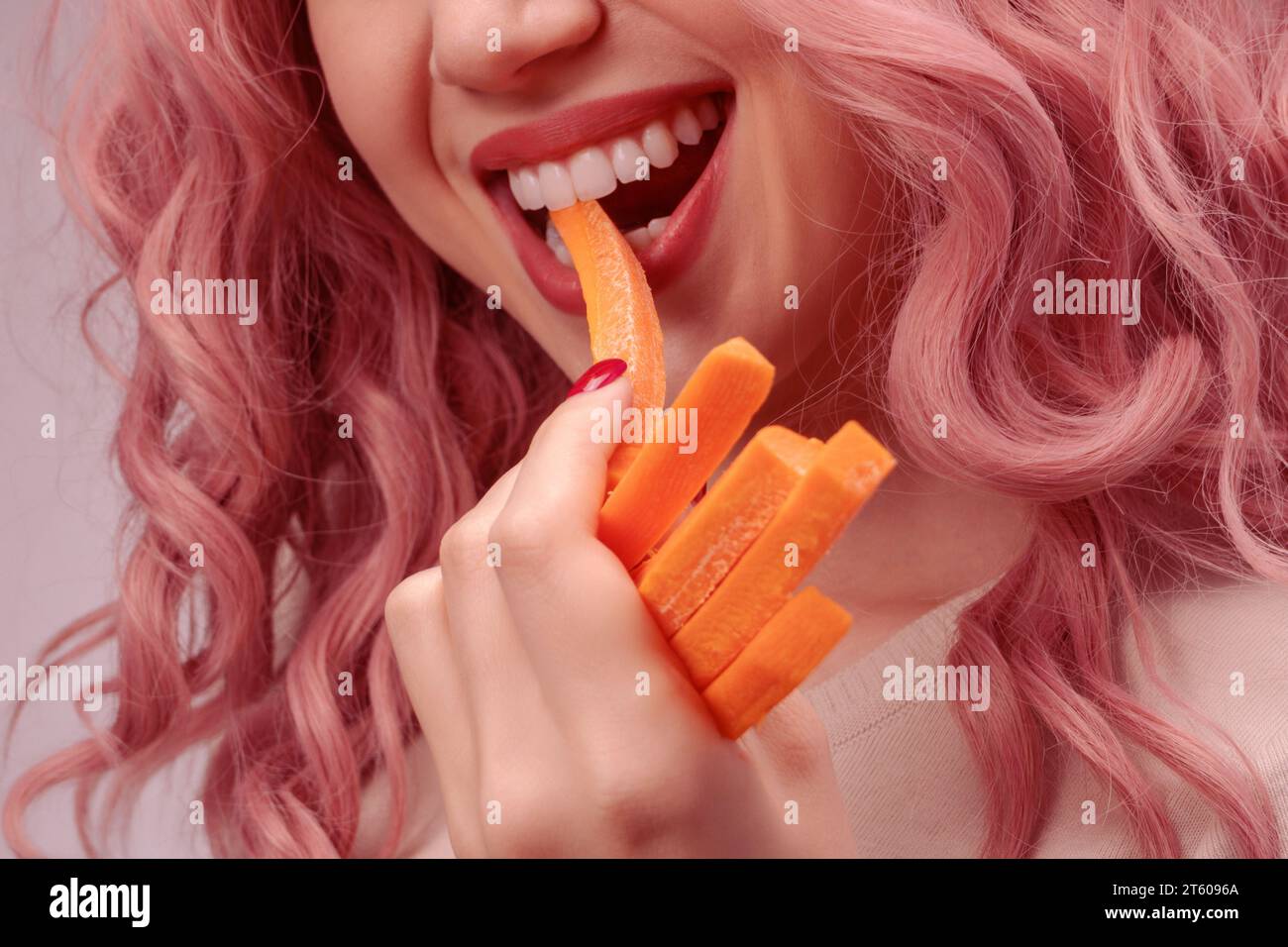 Carrots cut into strips in woman hand. Woman with pink curly hair is ...