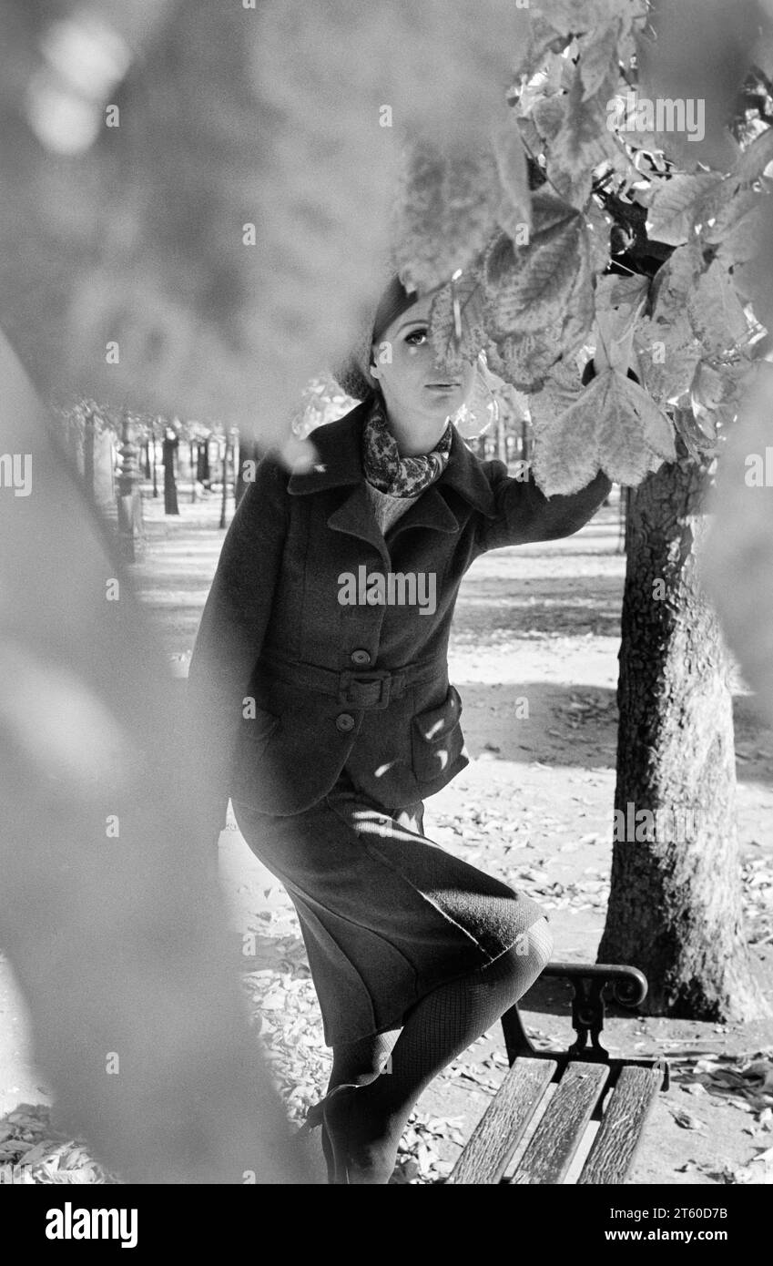 1960s, woman fashion model standing on bench, tree autumnal leaves ...