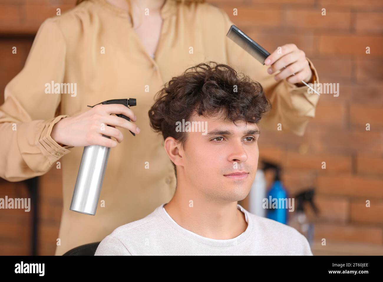 Professional hairdresser applying hair spray on young man's curly hair ...