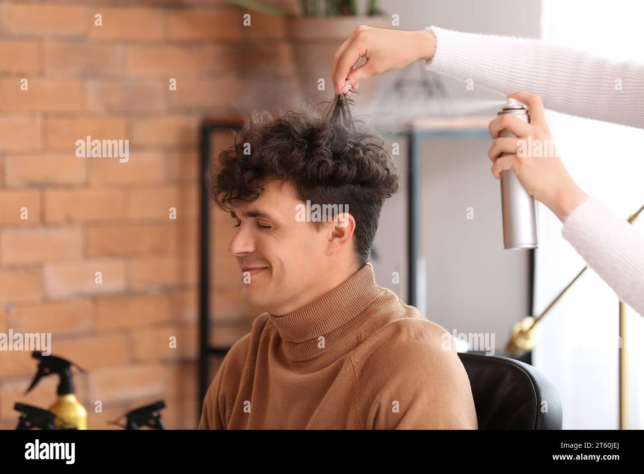 Professional hairdresser applying hair spray on young man's curly hair ...
