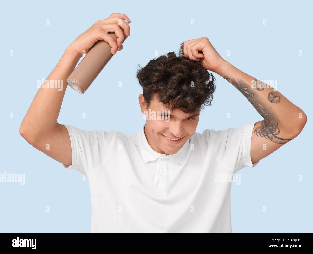 Handsome young man applying hair spray on his curly hair against blue ...