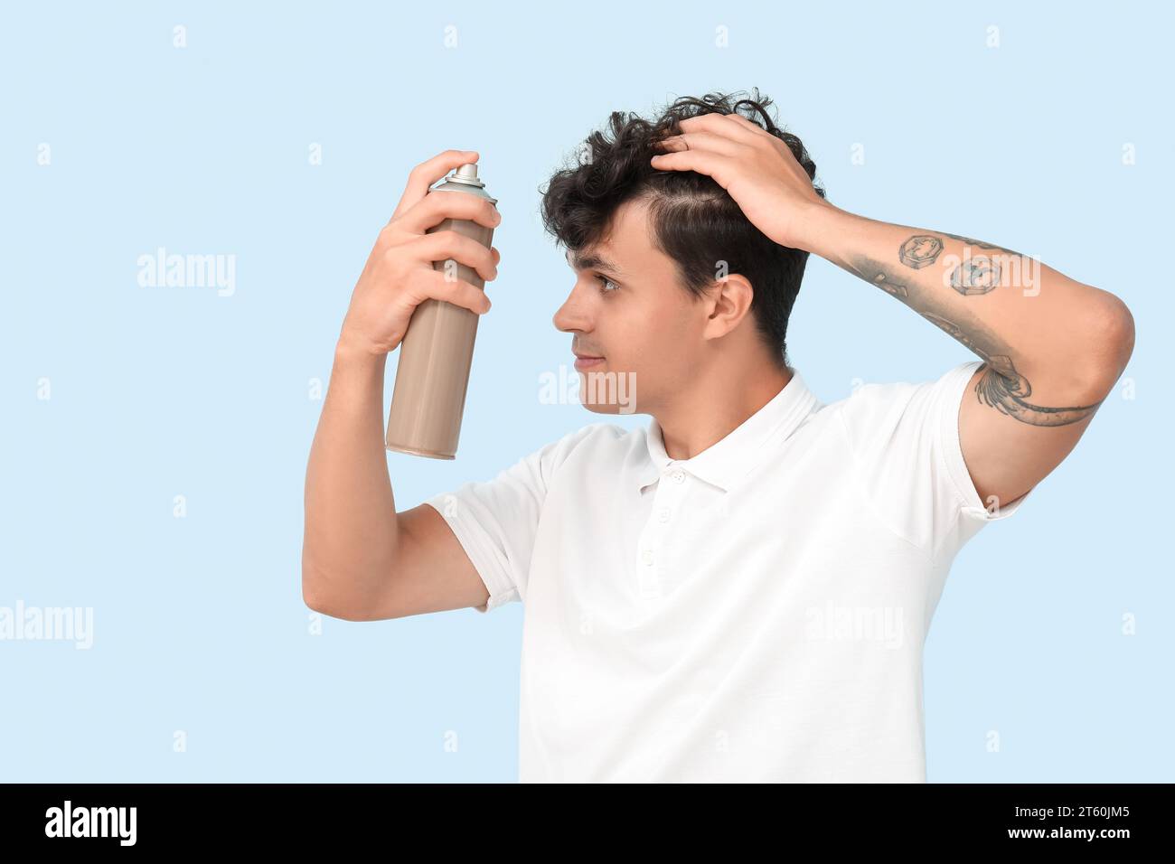 Handsome young man applying hair spray on his curly hair against blue ...