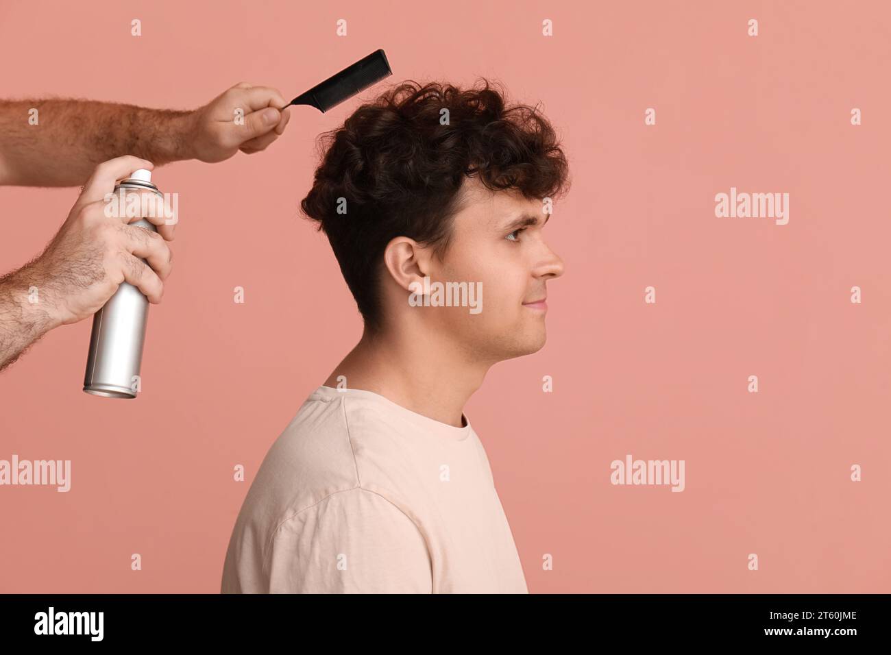 Professional hairdresser applying hair spray on young man's curly hair ...