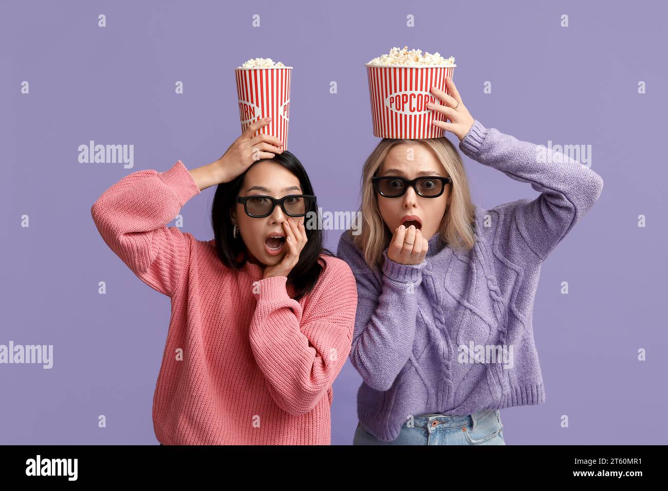 Emotional young women in 3D glasses with buckets of popcorn on purple background Stock Photo - Alamy
