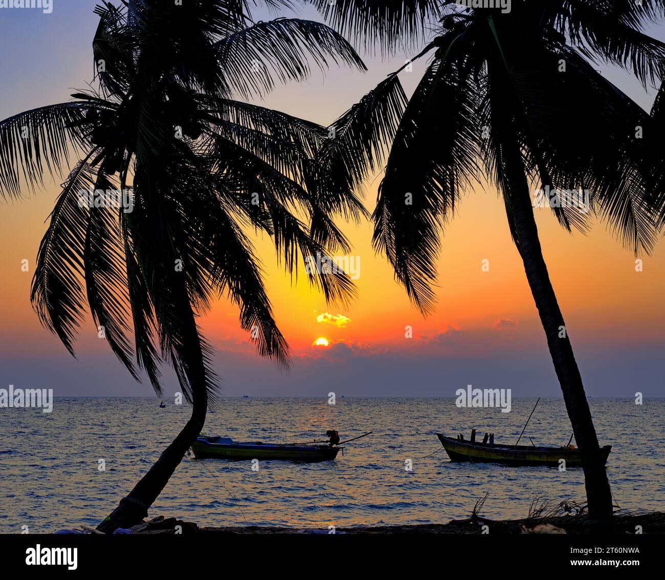Sunrise from the sea with two coconut trees and two floating boats in ...