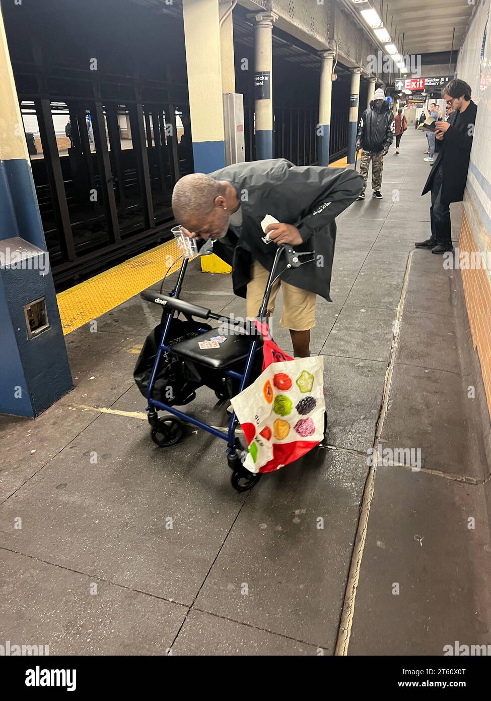 Severely bent over man leans on his walker along the subway platform at ...