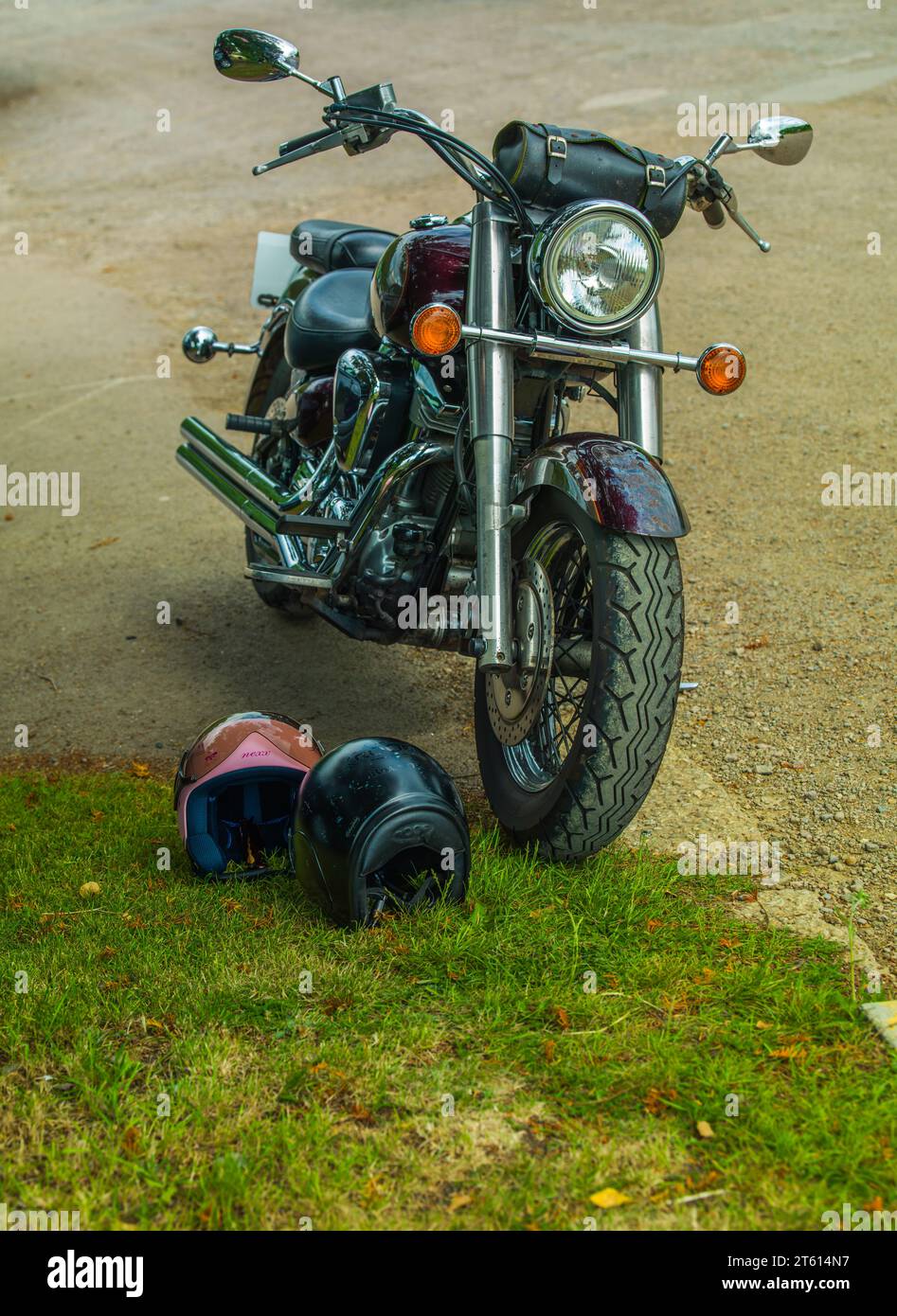 A motorycle on its stand with two crash helmets by the front wheel ...