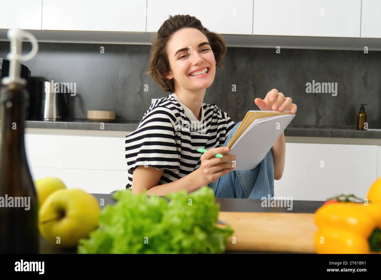 Portrait of young woman cooking, writing notes, grocery list in ...