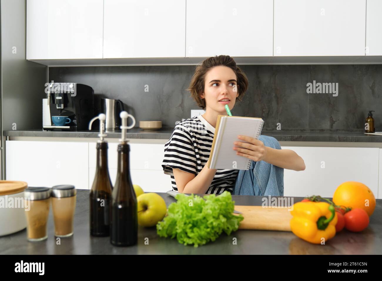 Portrait of thinking woman with notebook, cooking, writing down recipe ...