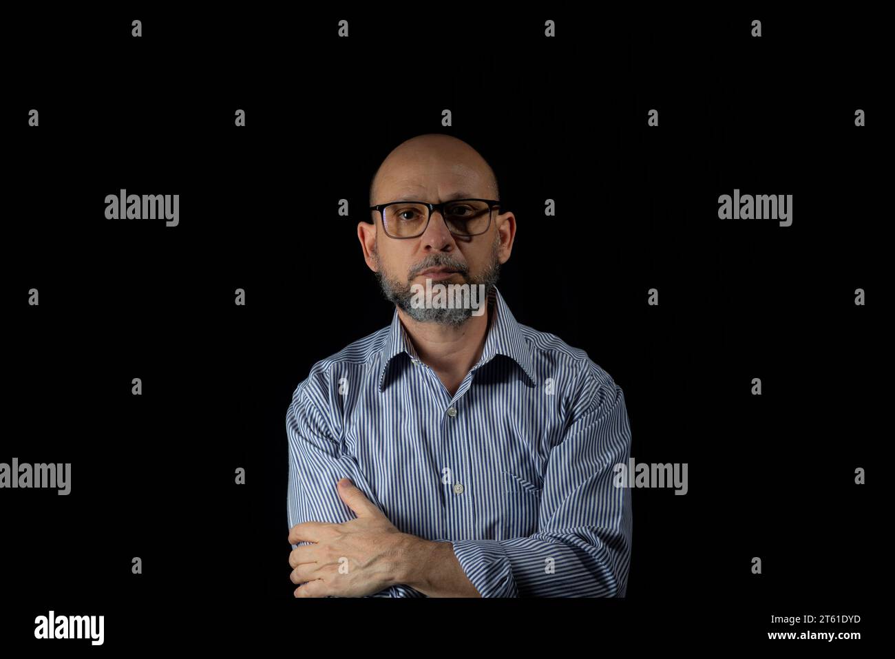 Serious, bald and bearded man looking at the camera against black ...