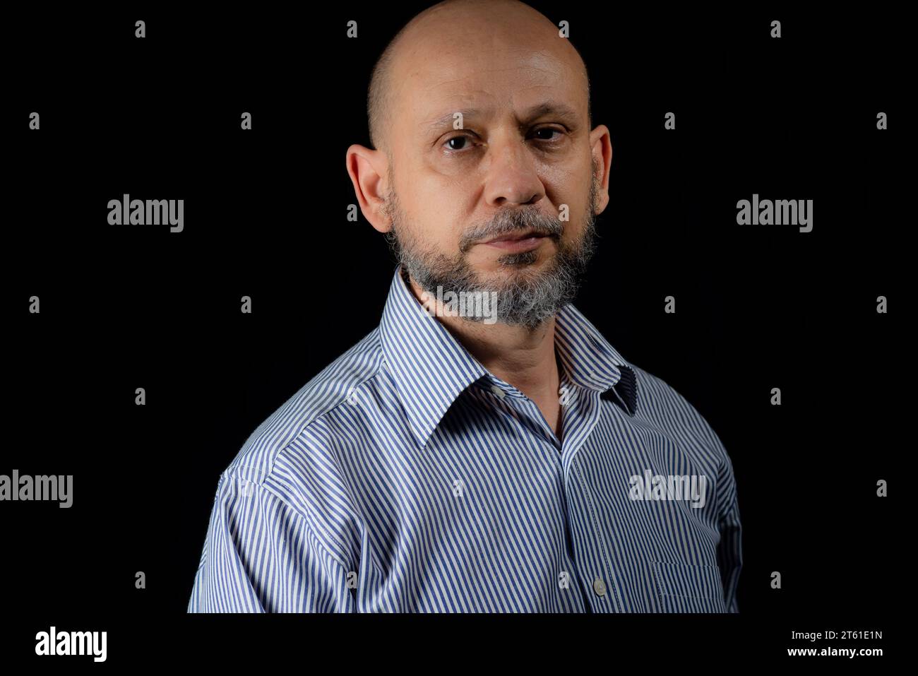 Serious, bald and bearded man looking at the camera against black ...