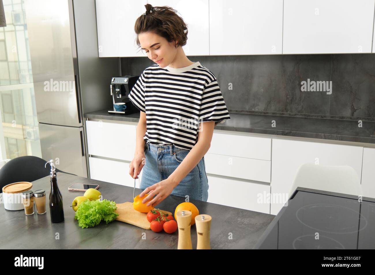 Portrait of modern young woman standing in the kitchen with vegetables ...