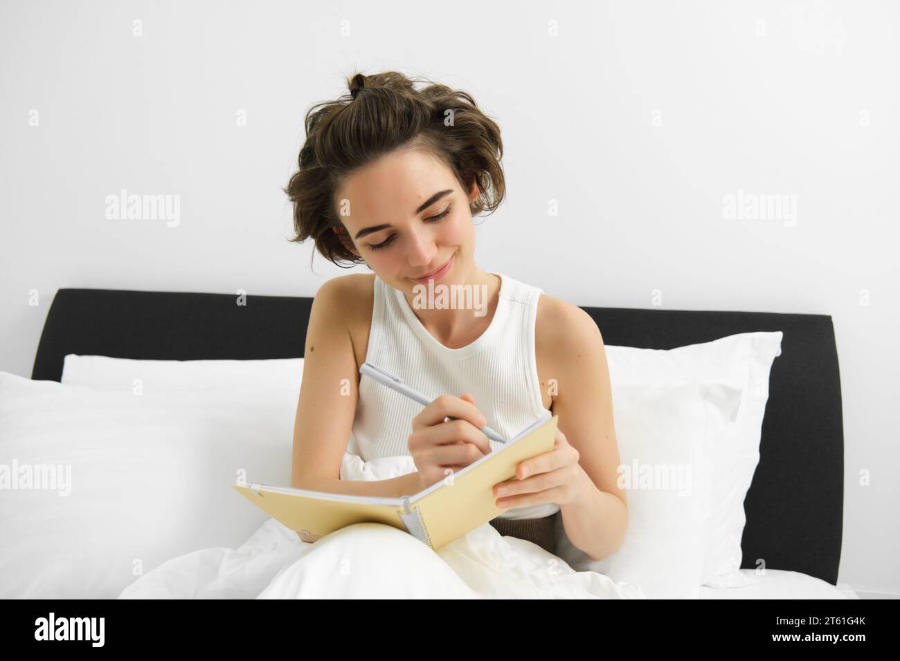 Image of mindful young woman sitting in bed, waking up and writing in ...