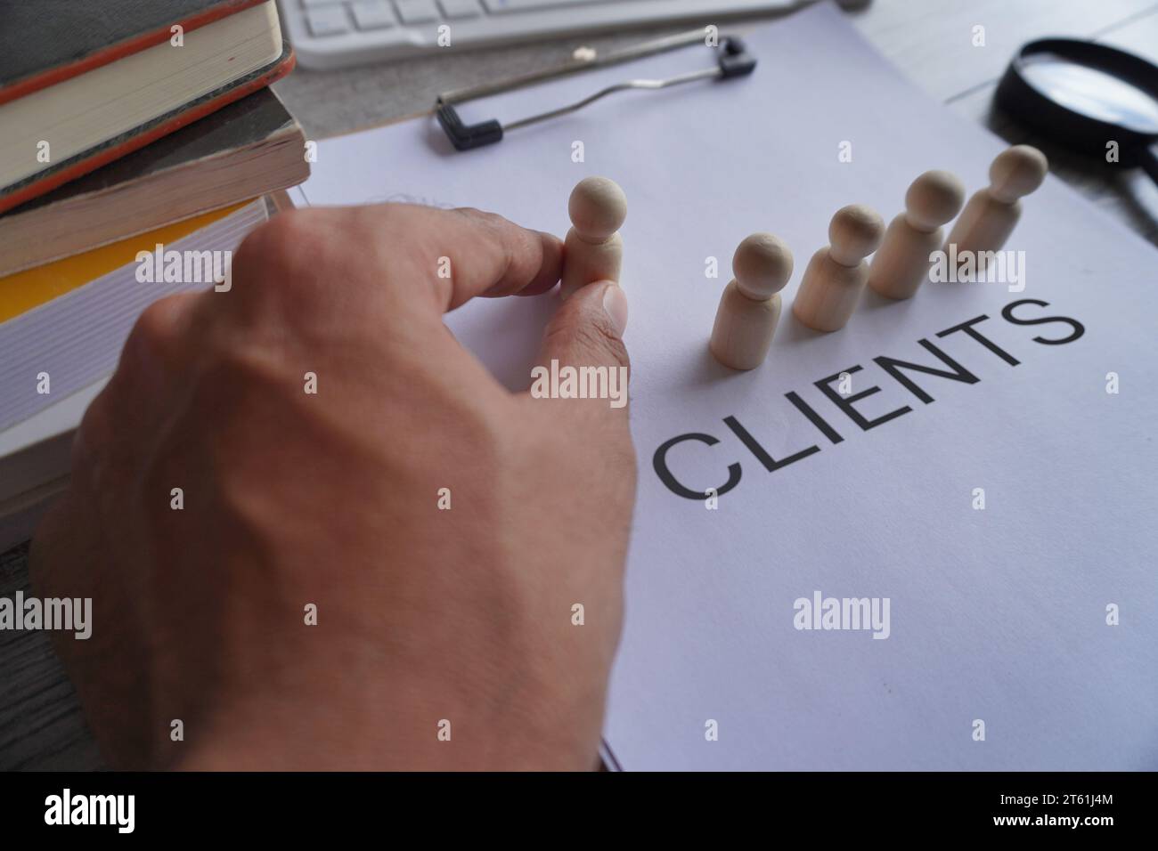 Hand holding wooden doll and paper clipboard with text CLIENTS ...