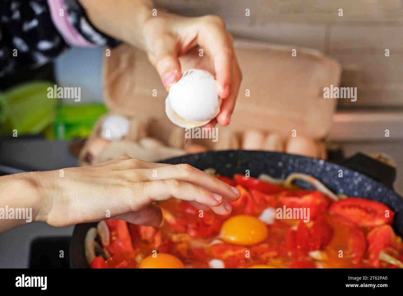 girl holds a chicken egg in her hand to break it. cooking scrambled eggs with tomatoes Stock ...