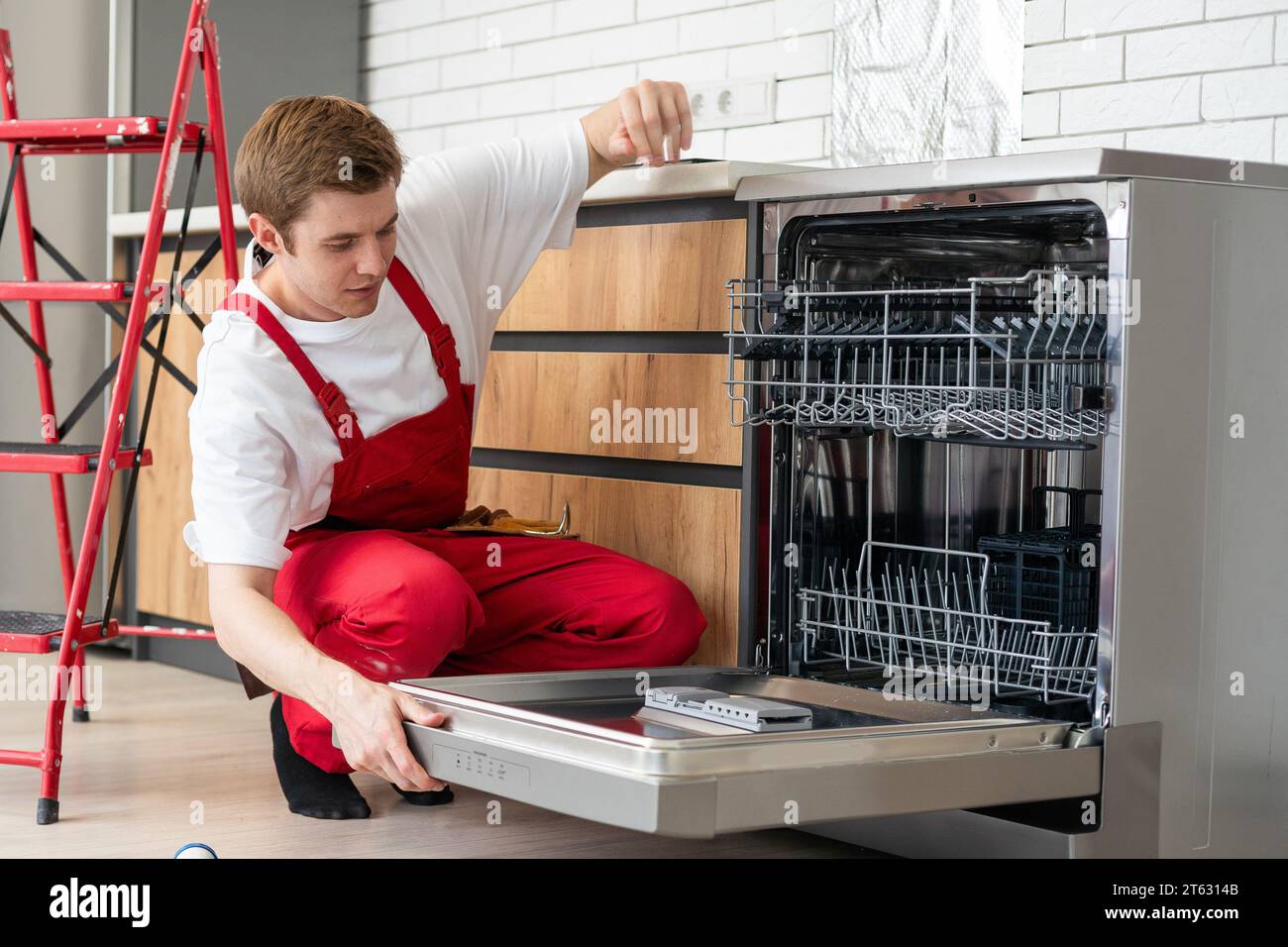 Technician or worker in uniform installs dishwasher into the kitchen ...