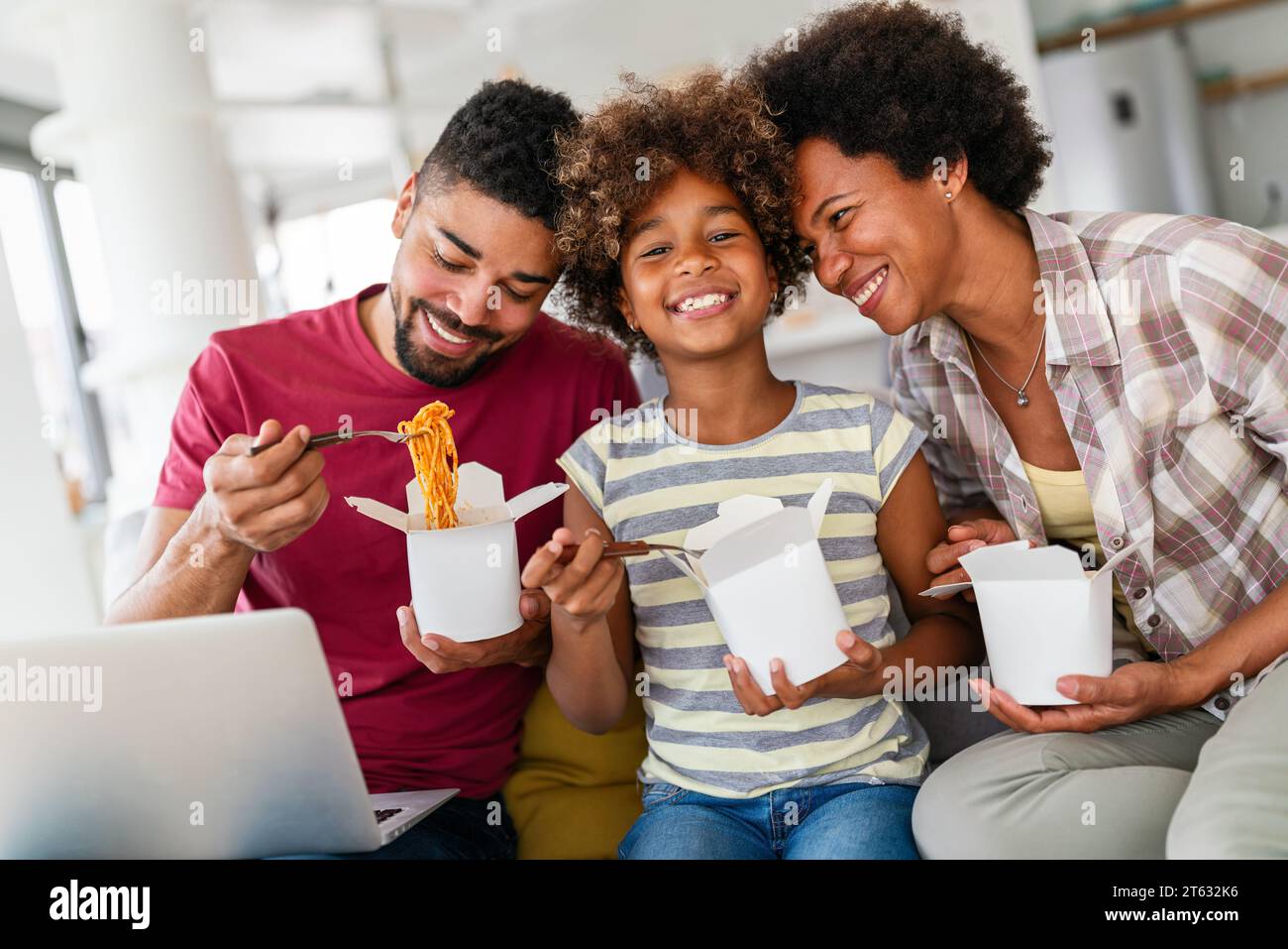 Happy african american family eating on couch with cardboard boxes in ...