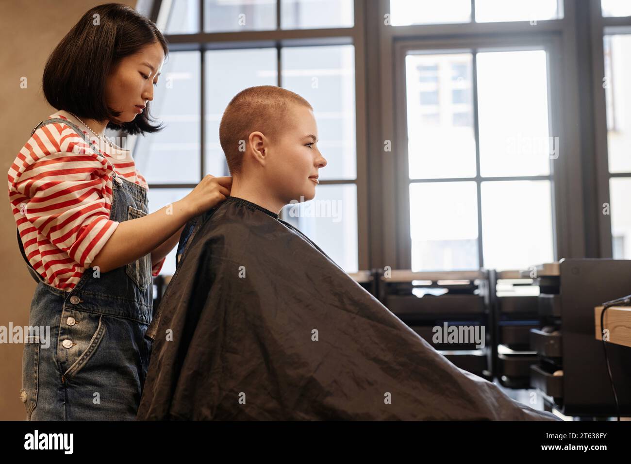 Side view portrait of smiling young woman with buzzcut sitting in salon ...