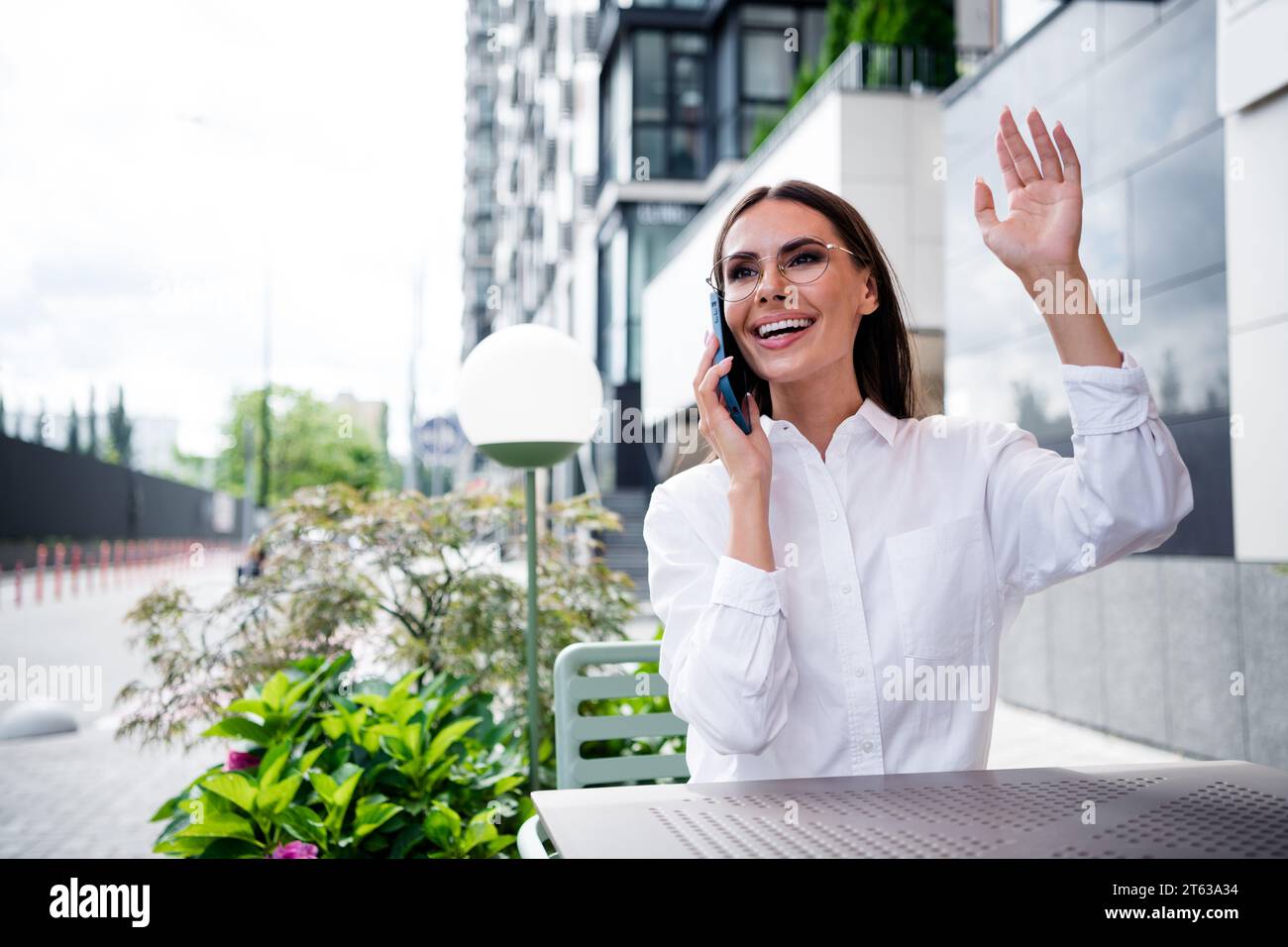 Photo of attractive elegant girl sit cafe table speak telephone arm palm waving hi call waiter ...