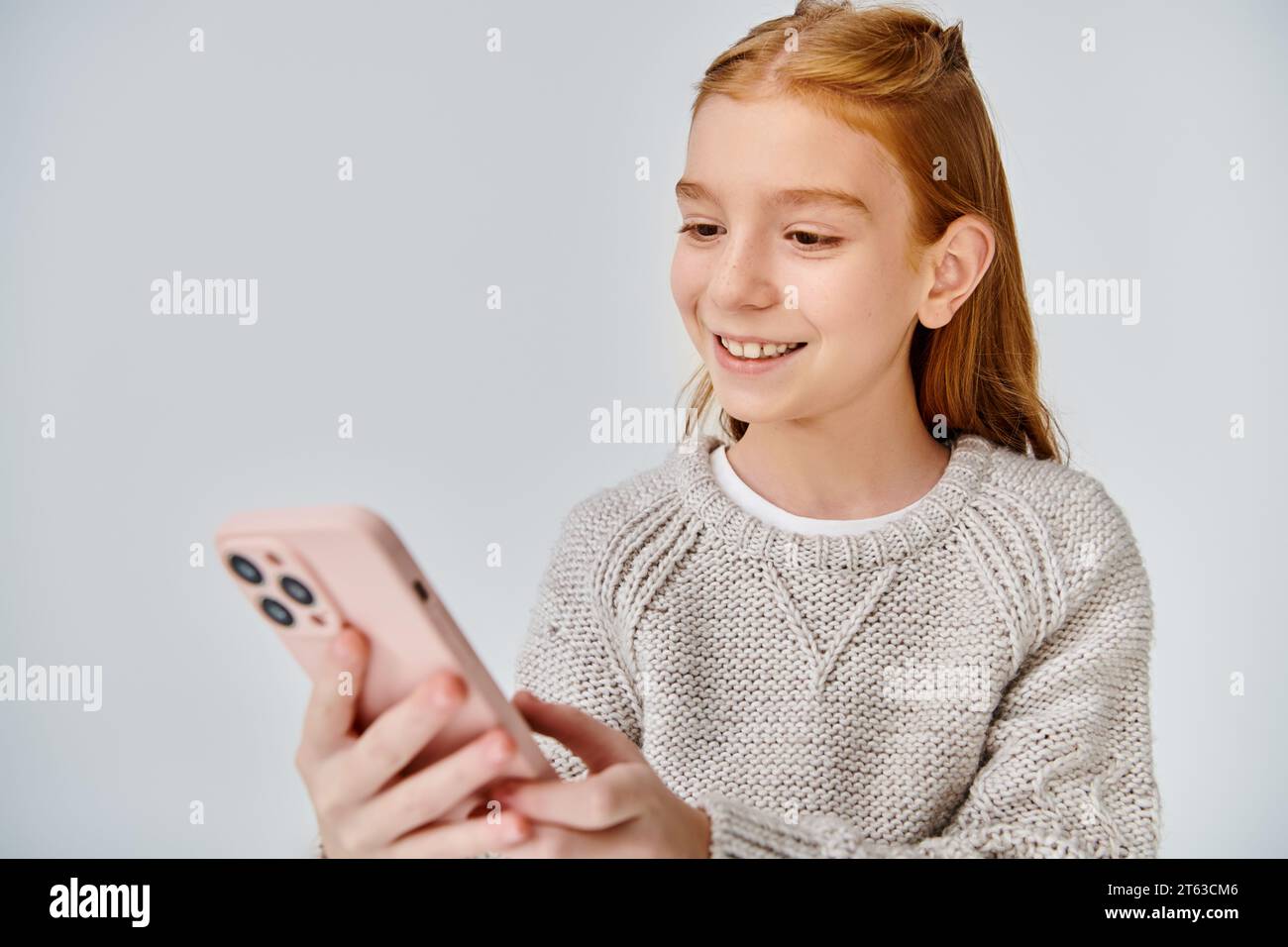cheerful preteen girl with red hair looking joyfully at her phone on ...