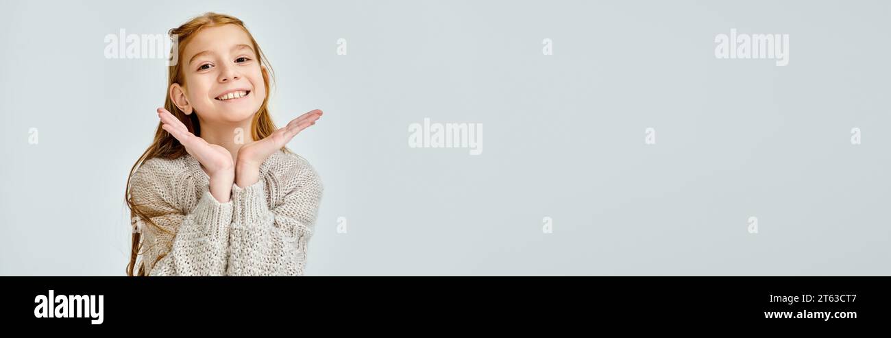 pretty little girl in casual sweater looking at camera, hands under ...