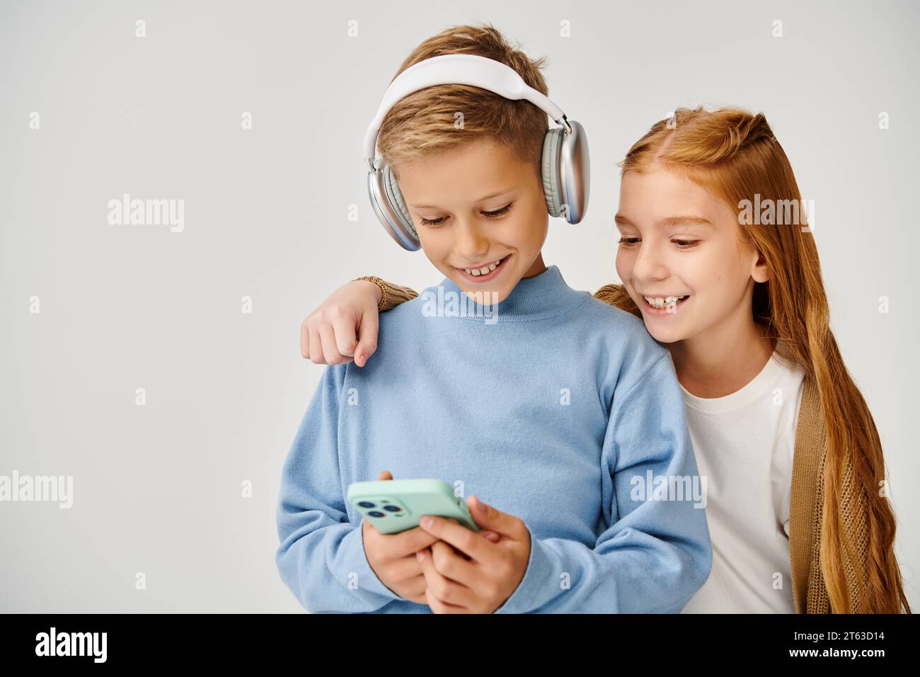 red haired jolly preteen girl looking at phone of her cute peer with ...