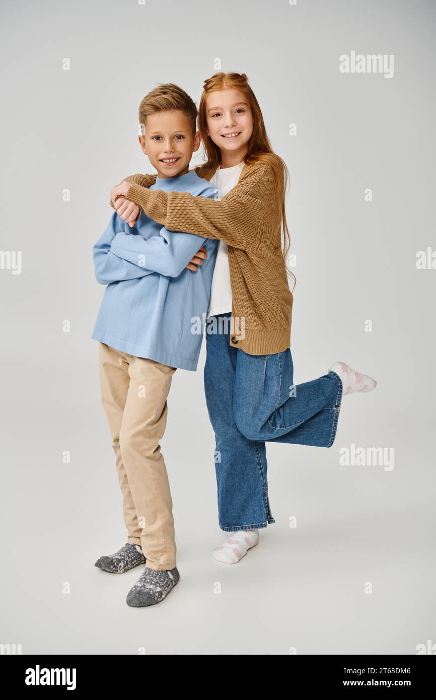 little girl in knitted cardigan raising one leg and hugging her preteen ...