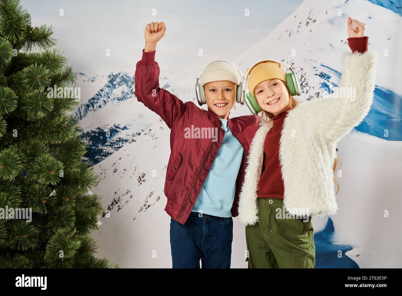 joyous little children in stylish jackets cheering with raised arms ...