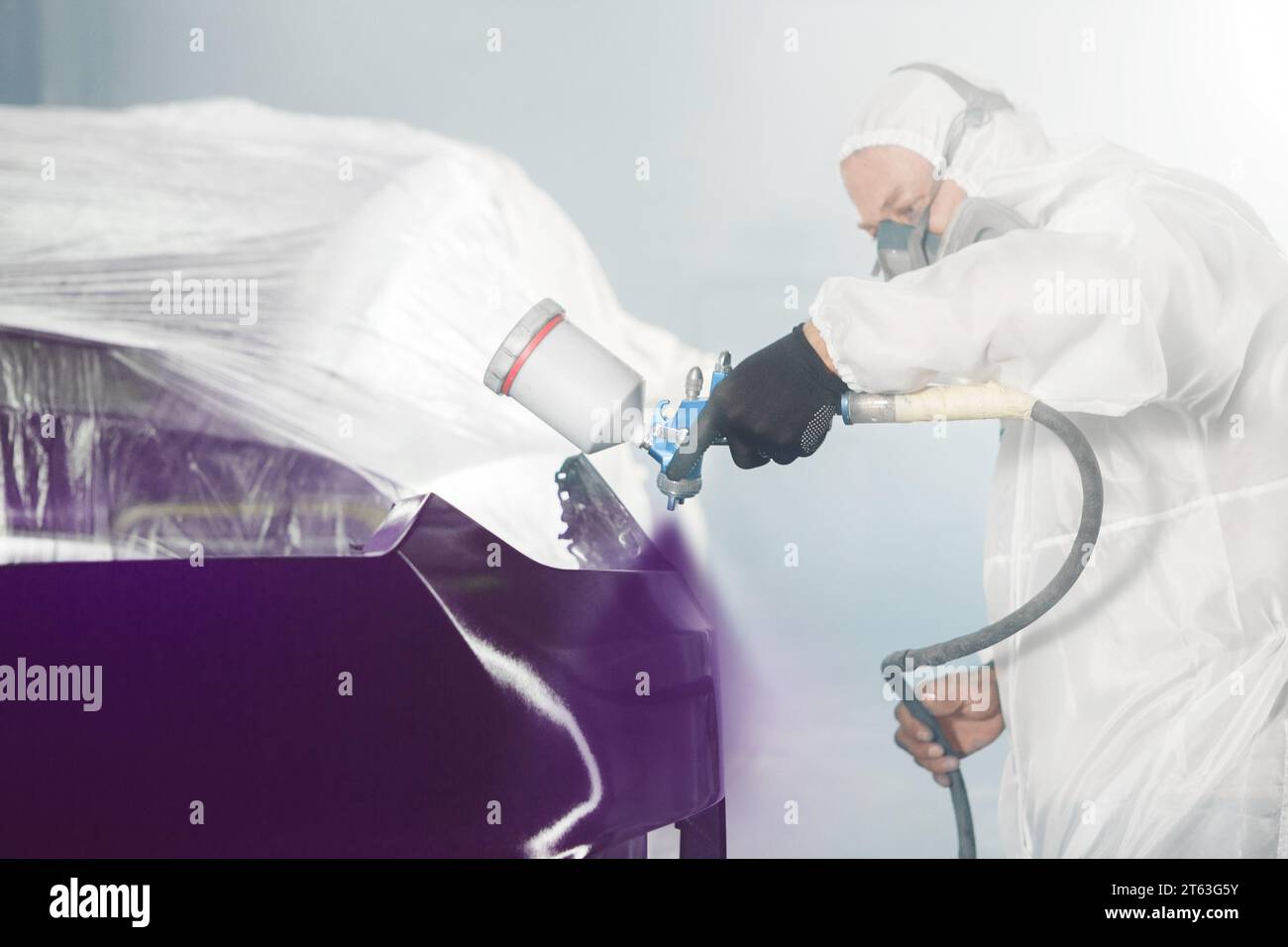 Car paint worker spraying purple paint to car body element using spray ...