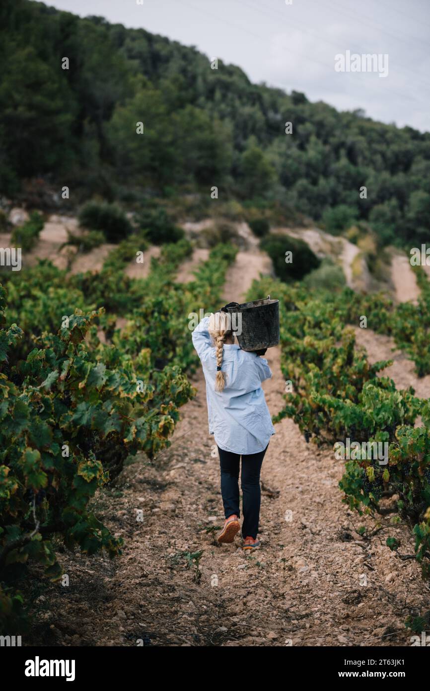 Back view of anonymous female farmer wearing casual attire carrying ...