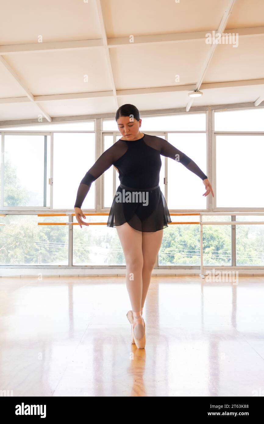 Focused ballet dancer in a black leotard and sheer skirt gracefully ...