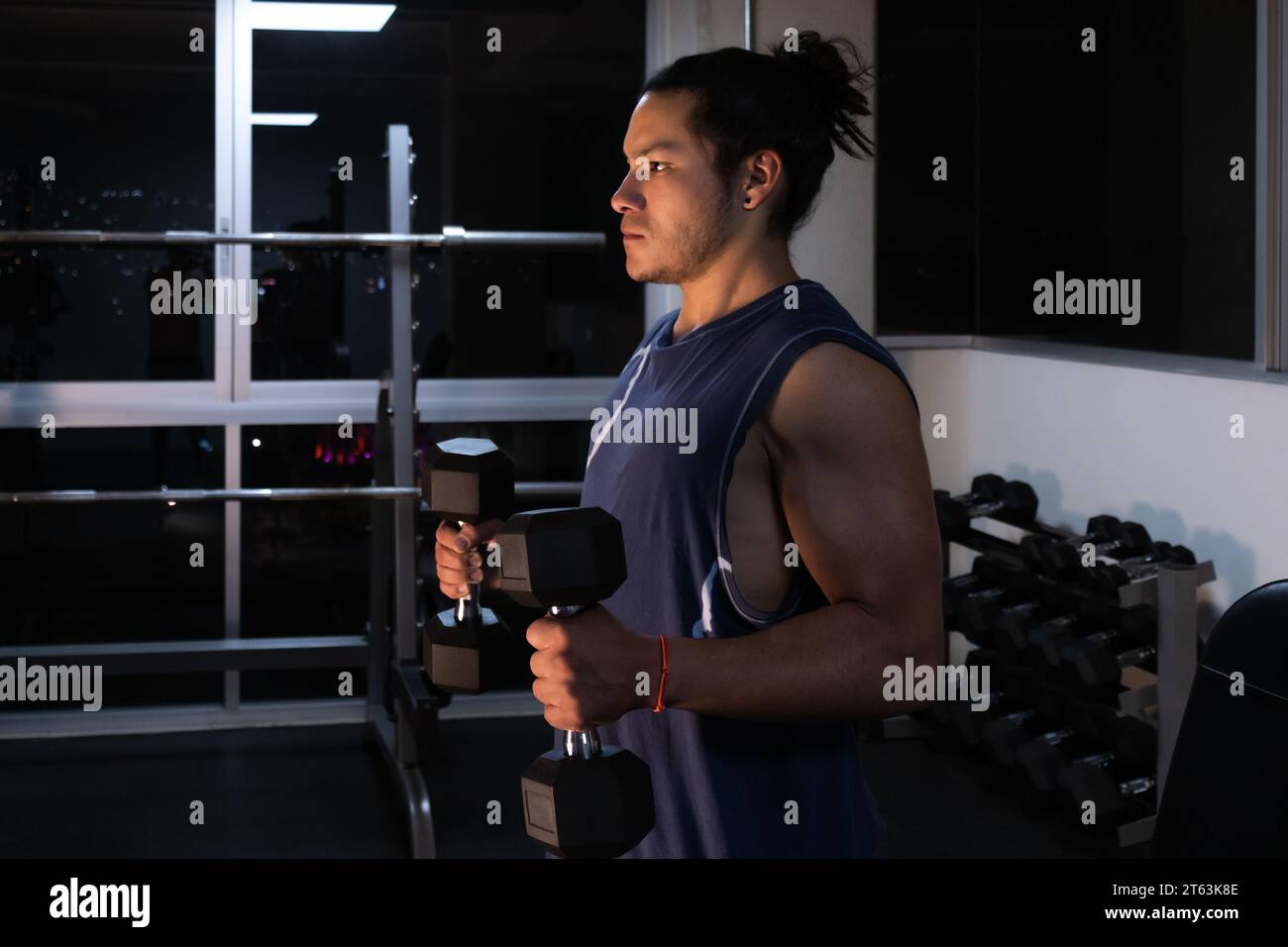 Side view of focused man lifts dumbbells in a dimly lit gym with the ...