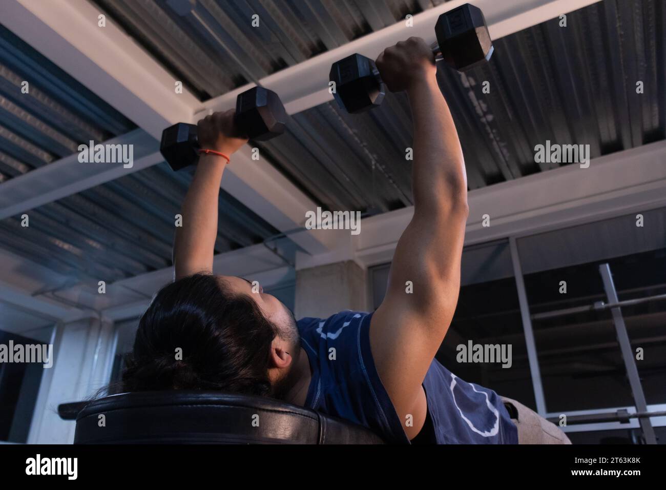 A man performing a chest press exercise with dumbbells in a gym ...
