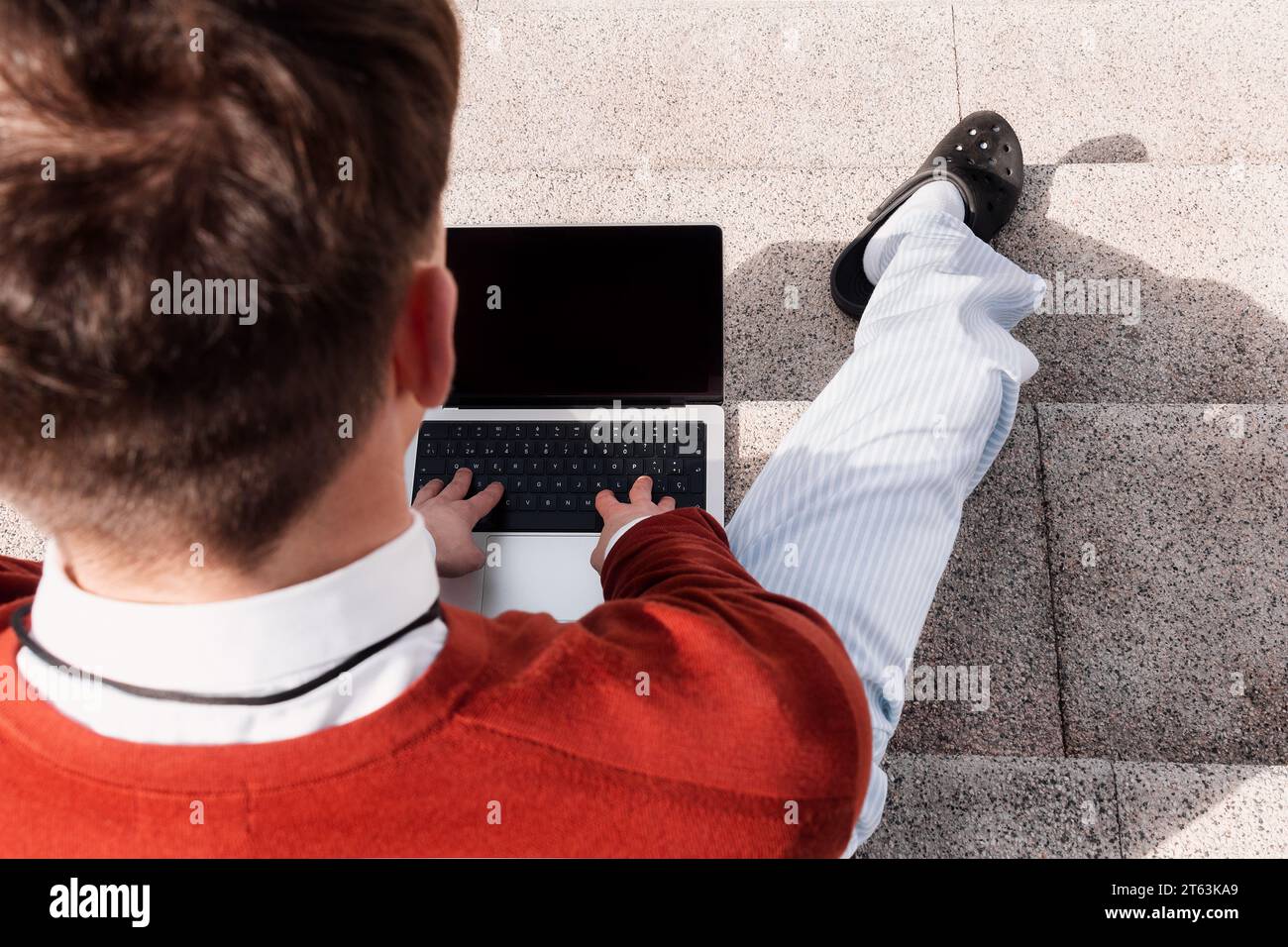 Overhead view of a gen-z man working on a laptop outdoors on city steps ...